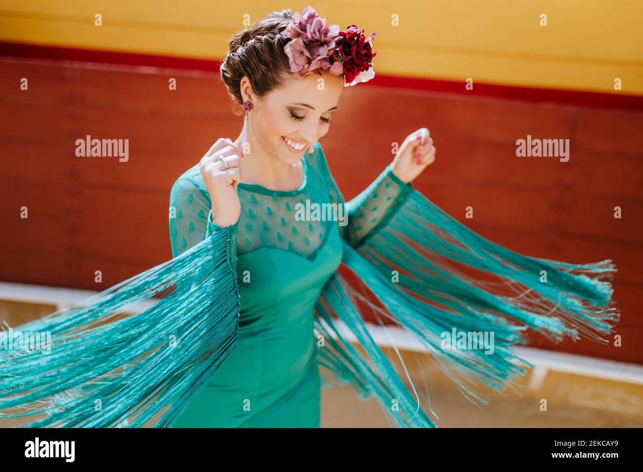 Smiling young woman wearing blue dress and flowers dancing in bullring ...