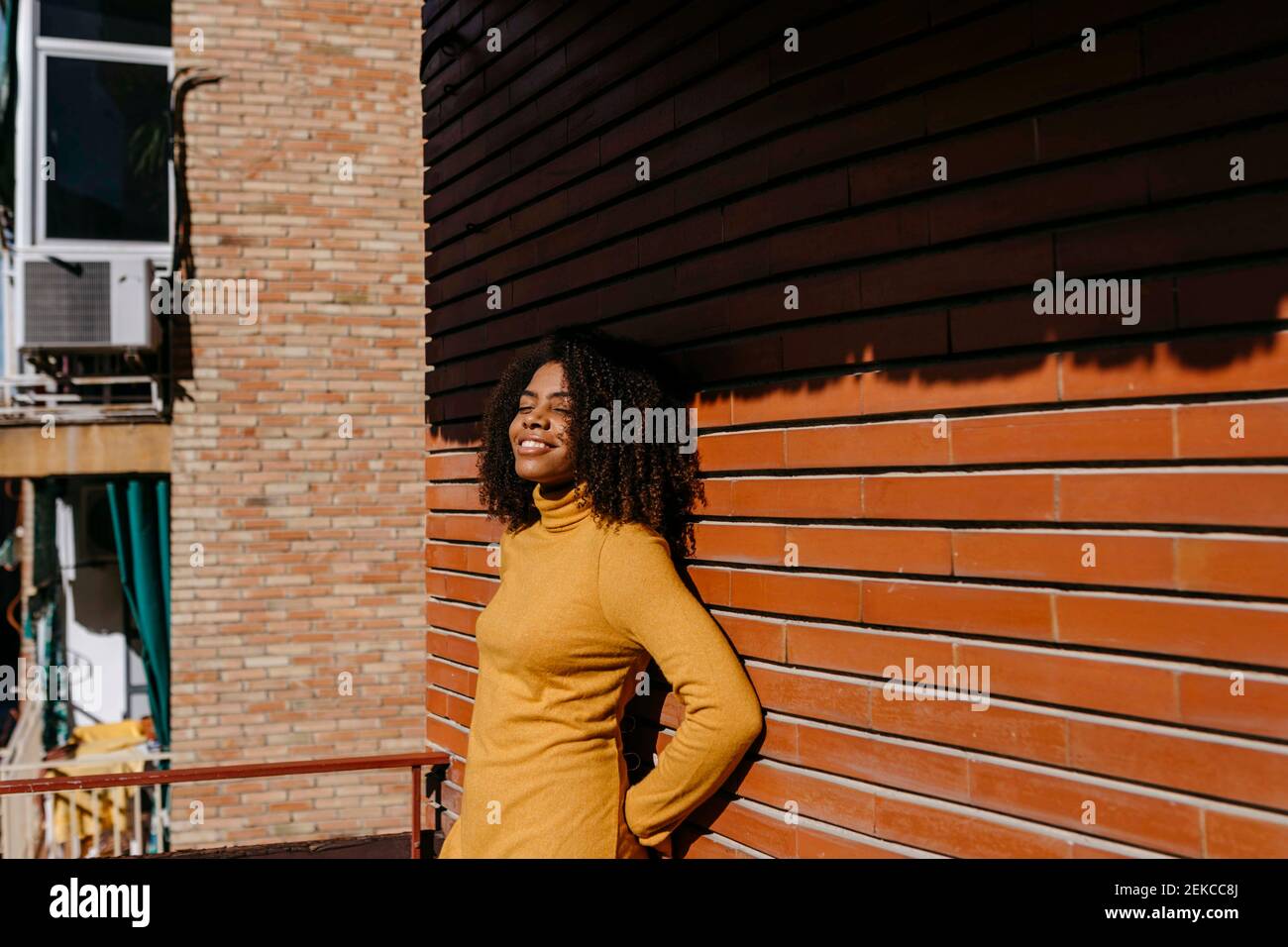 Smiling woman with hands behind back leaning on wall Stock Photo - Alamy