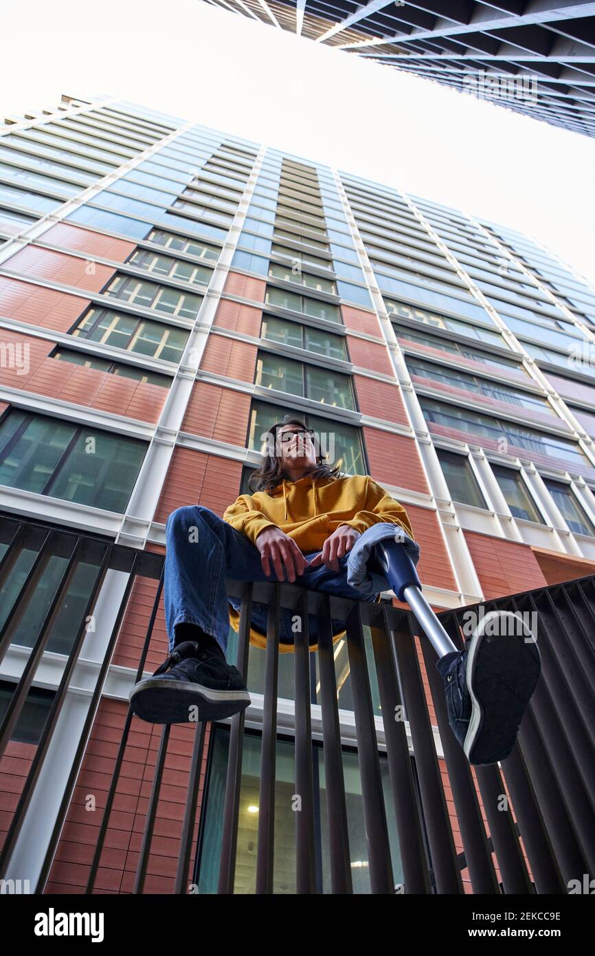 Disabled young man with leg prosthesis sitting on metal railing against ...