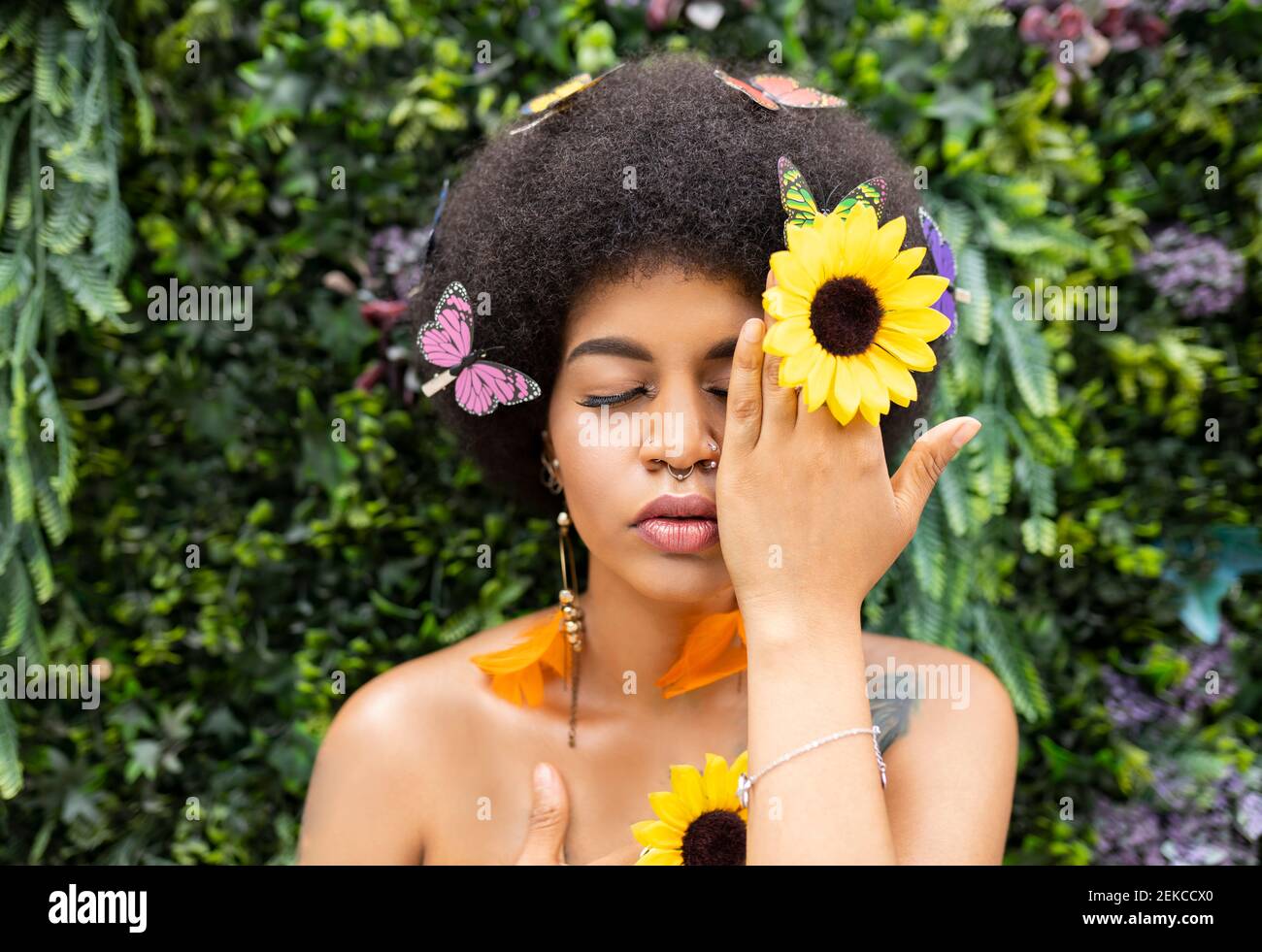 Afro woman covering eye with hand against plant Stock Photo - Alamy