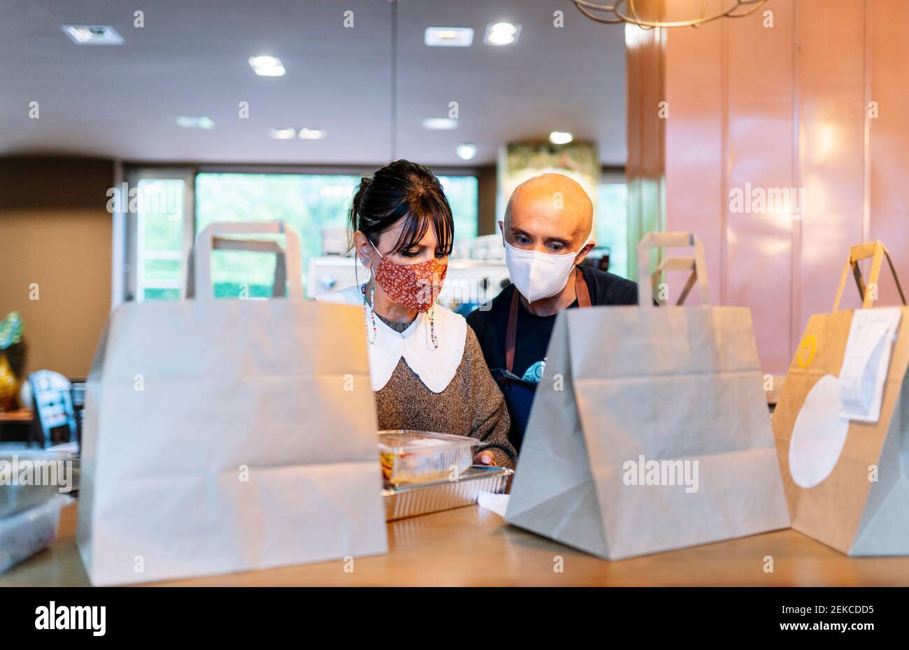 Female owner with male colleague preparing take out food on bar counter ...