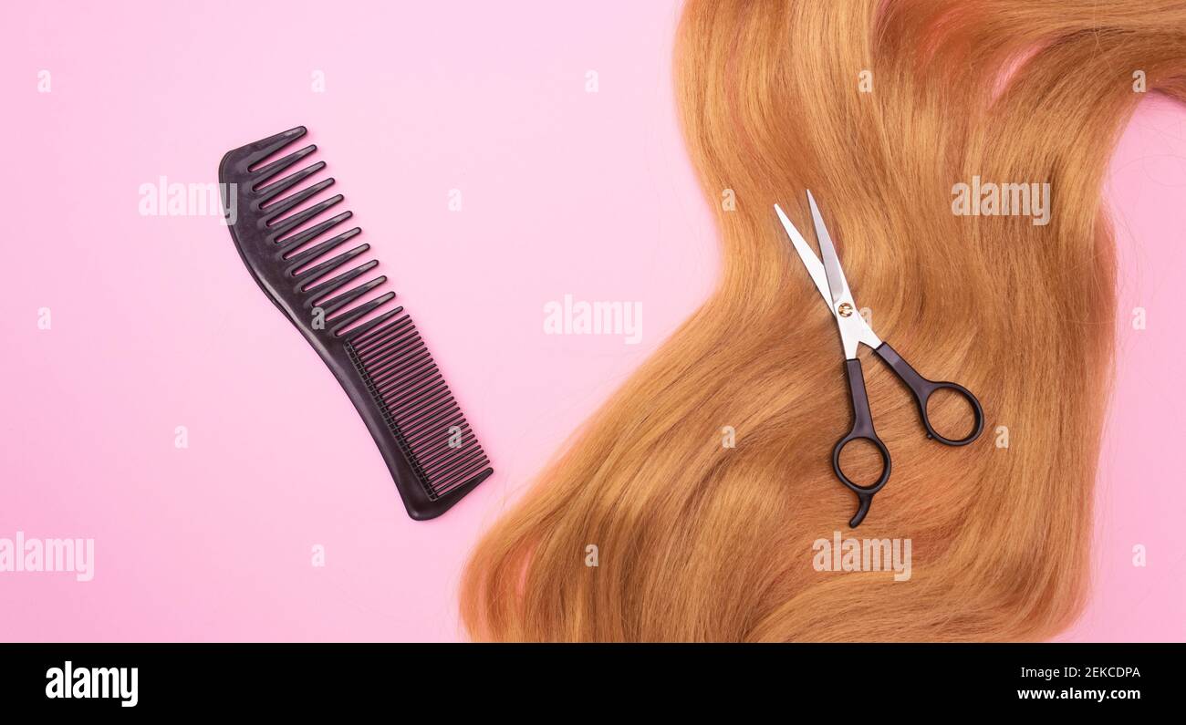 Red artificial hair on a pink background, comb and scissors. The ...