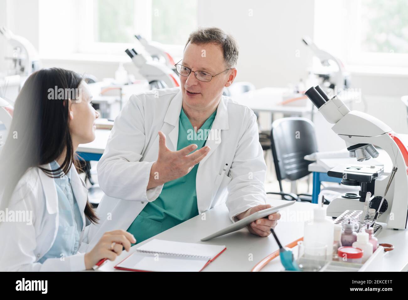 Teacher and student in white coats talking and using tablet in lab ...
