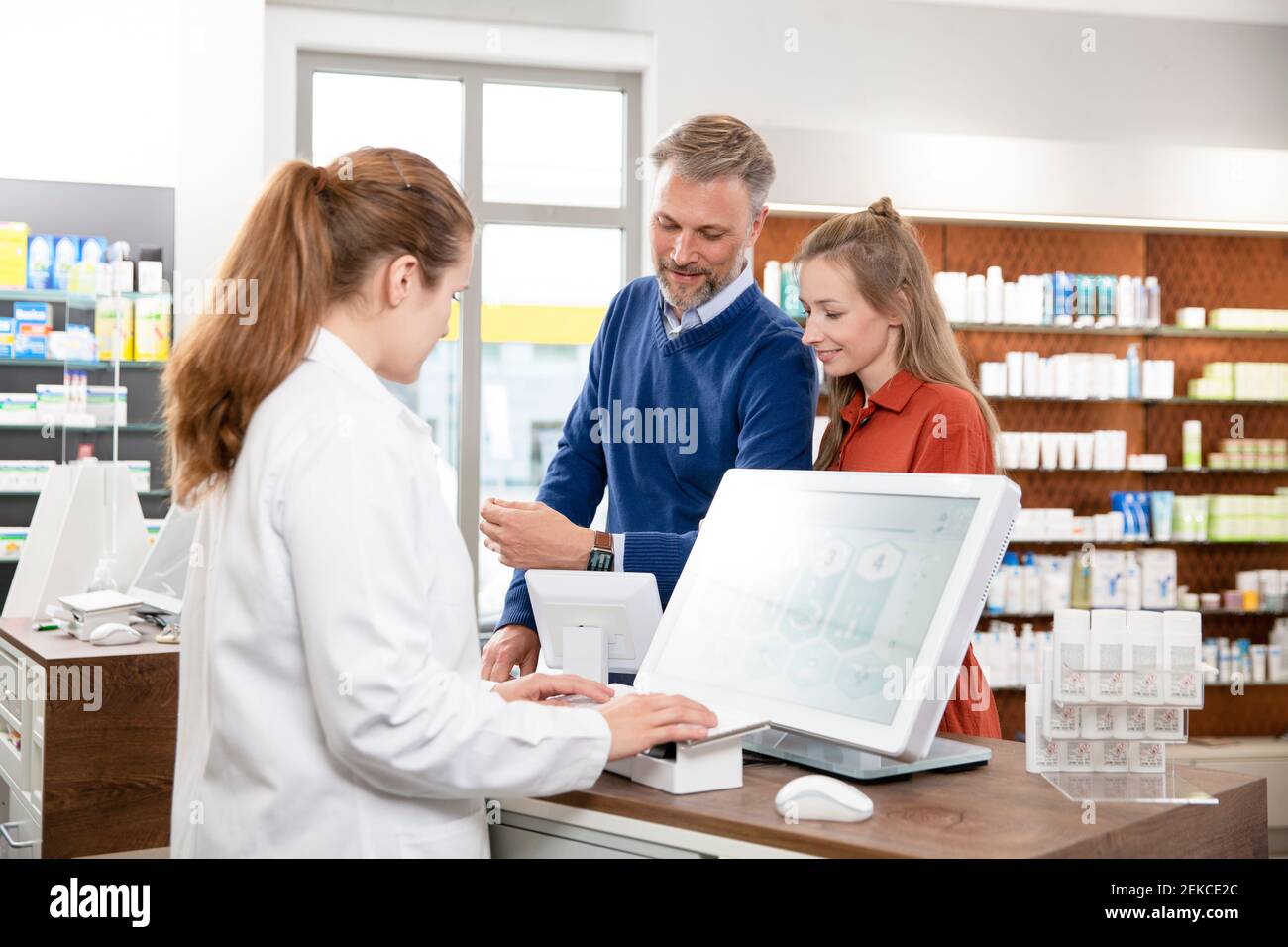 Female pharmacist billing while customers standing at pharmacy checkout ...