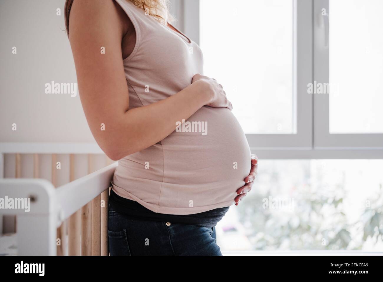 Pregnant woman with hands on stomach standing by window at home Stock ...