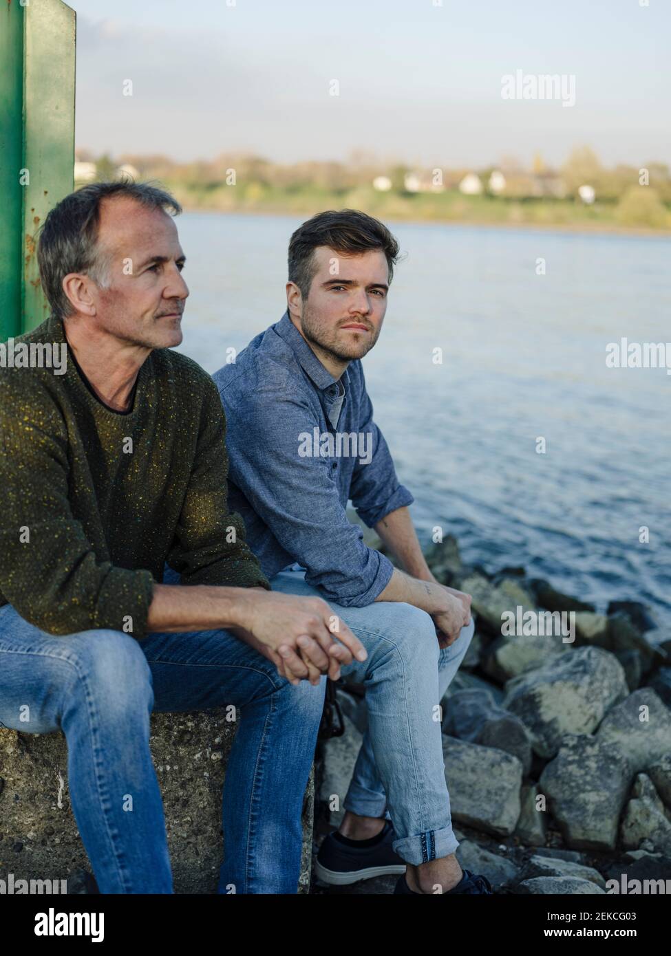 Father and son contemplating while sitting on rock against river Stock ...