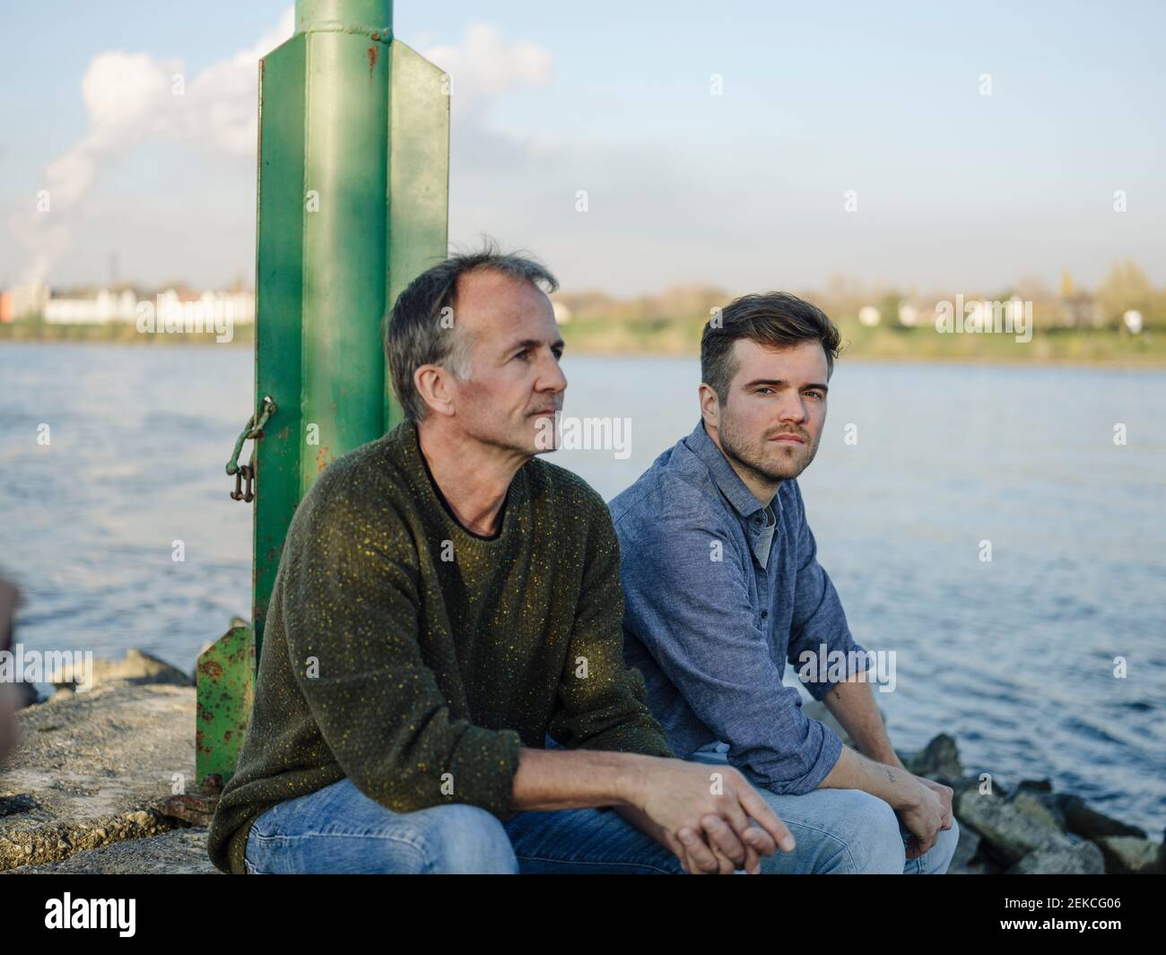 Thoughtful father and son sitting on rock against river Stock Photo - Alamy