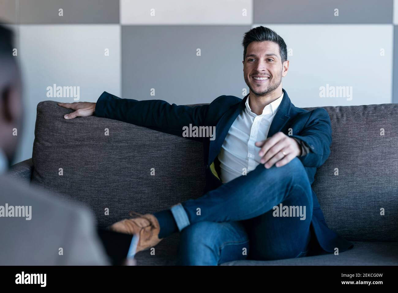 Confident businessman talking to colleague while sitting with legs ...