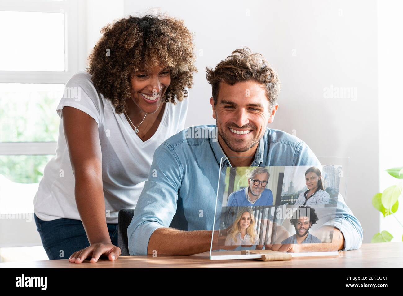 Couple talking with friends on video conference over transparent screen ...
