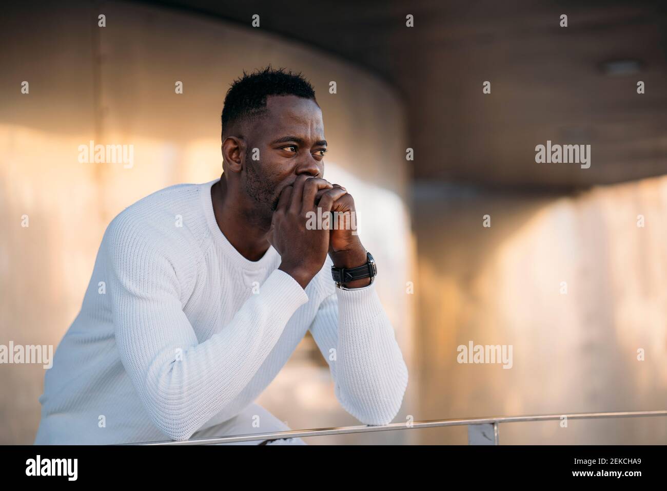 Thoughtful man with hands clasped leaning on railing while looking away ...