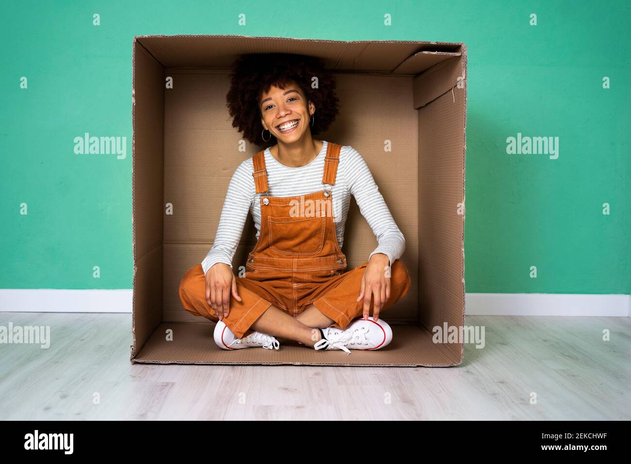 Happy young woman sitting with cross legs in cardboard box against ...