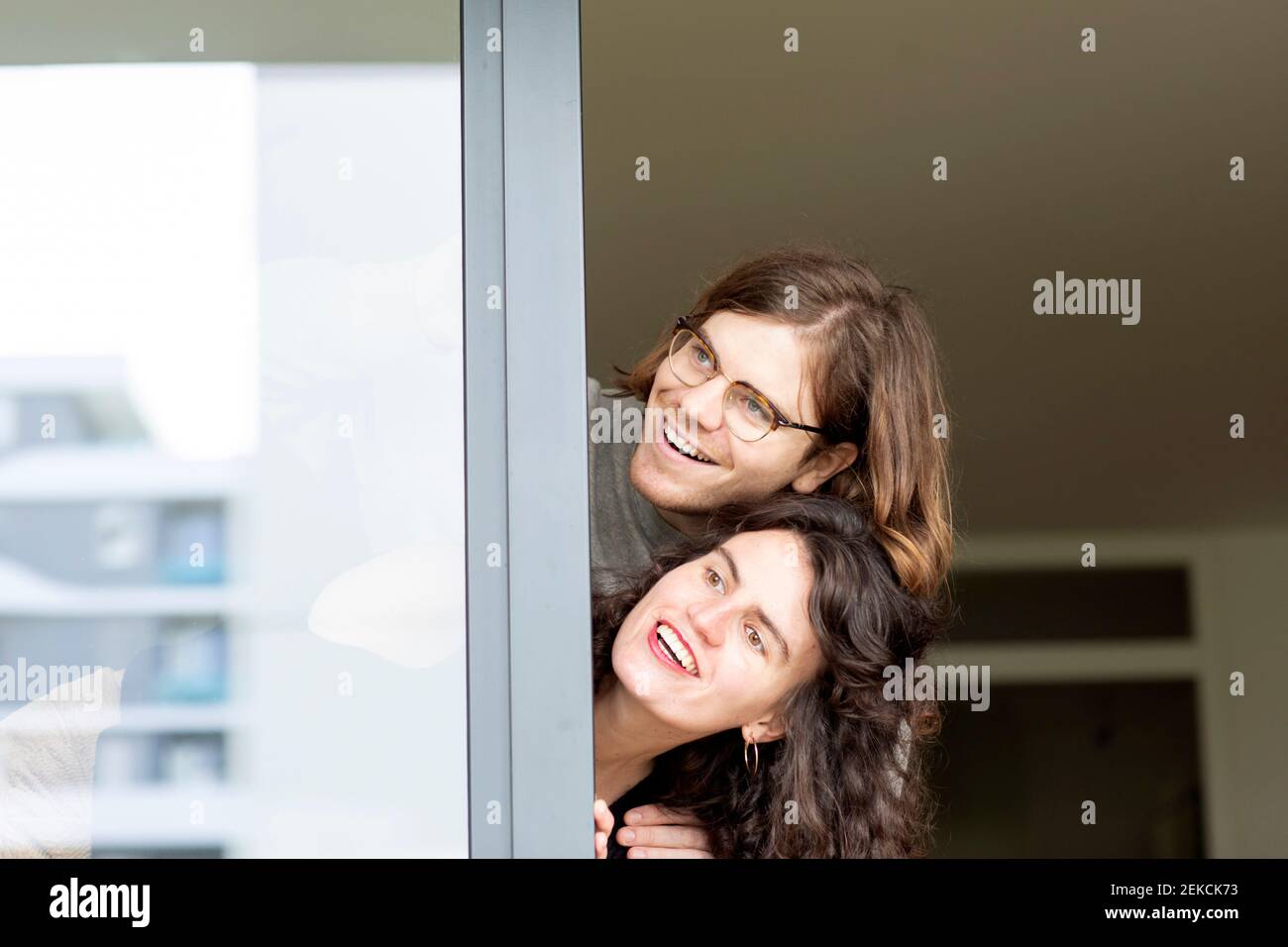 Smiling couple looking from behind glass window Stock Photo - Alamy