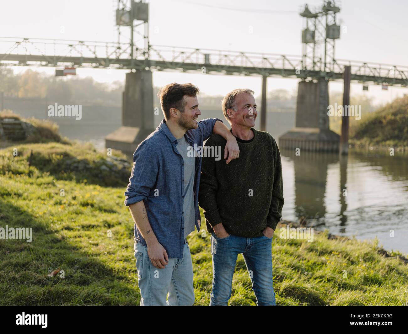 Son standing by smiling father at riverbank Stock Photo - Alamy