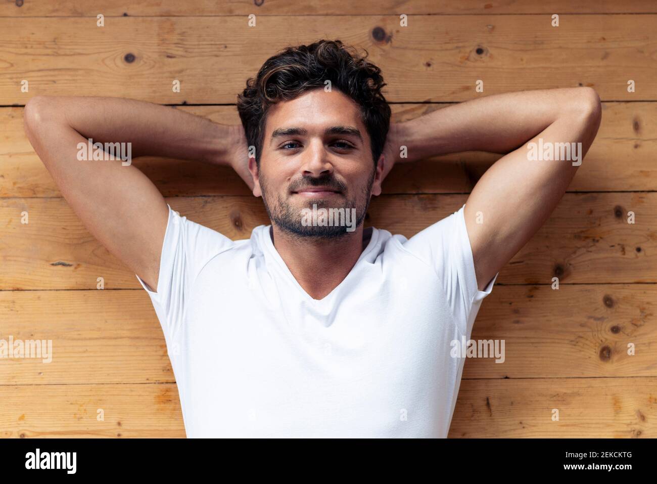 Mid adult man with hands behind head smiling while lying on floor at ...
