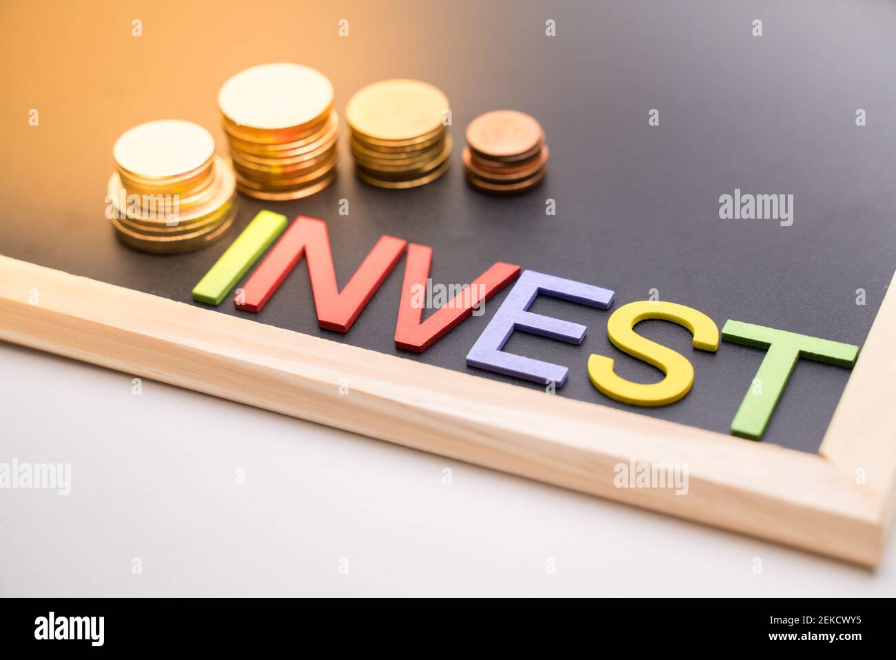 Invest text on blackboard with coin and light Stock Photo - Alamy