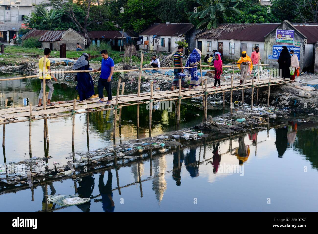 People crossing a river polluted with industrial garbage on a bamboo ...