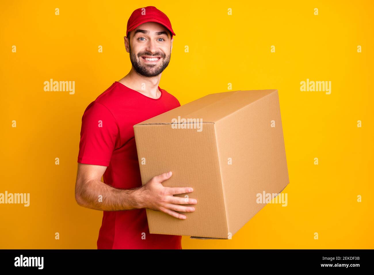 Photo of cute delivery man wear red outfit smiling holding big brown ...