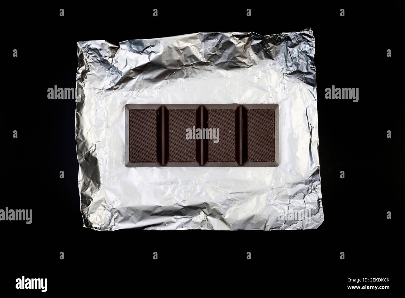 Sweet and delicious chocolate bar on silver foil on black background ...