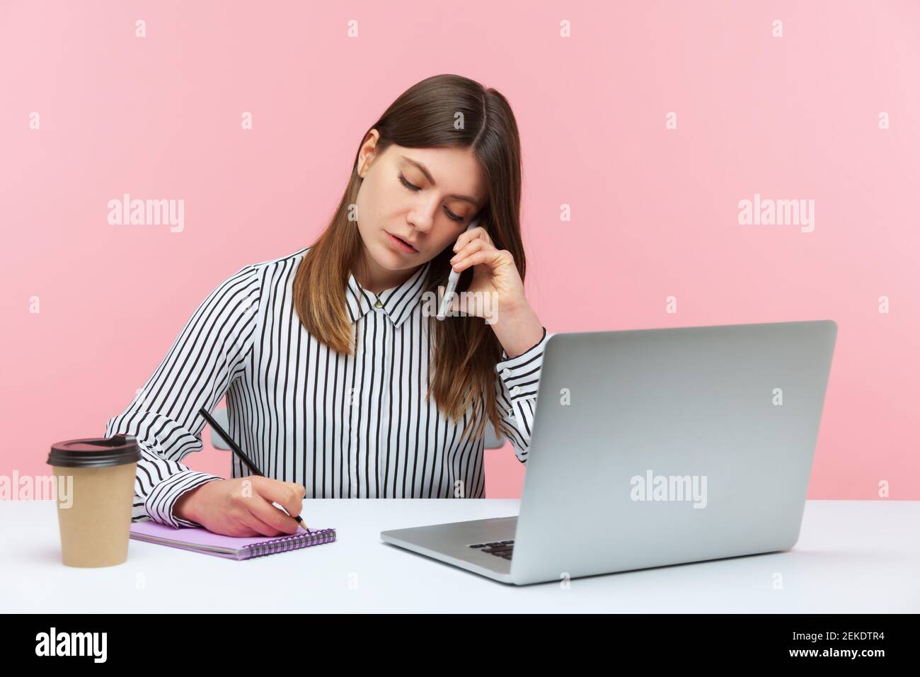 Diligent secretary in striped shirt receiving calls on phone and making ...