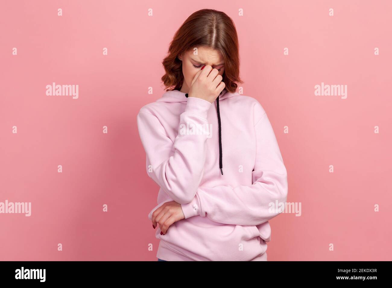 Portrait of upset young woman touching nose and frowning, wiping tears ...