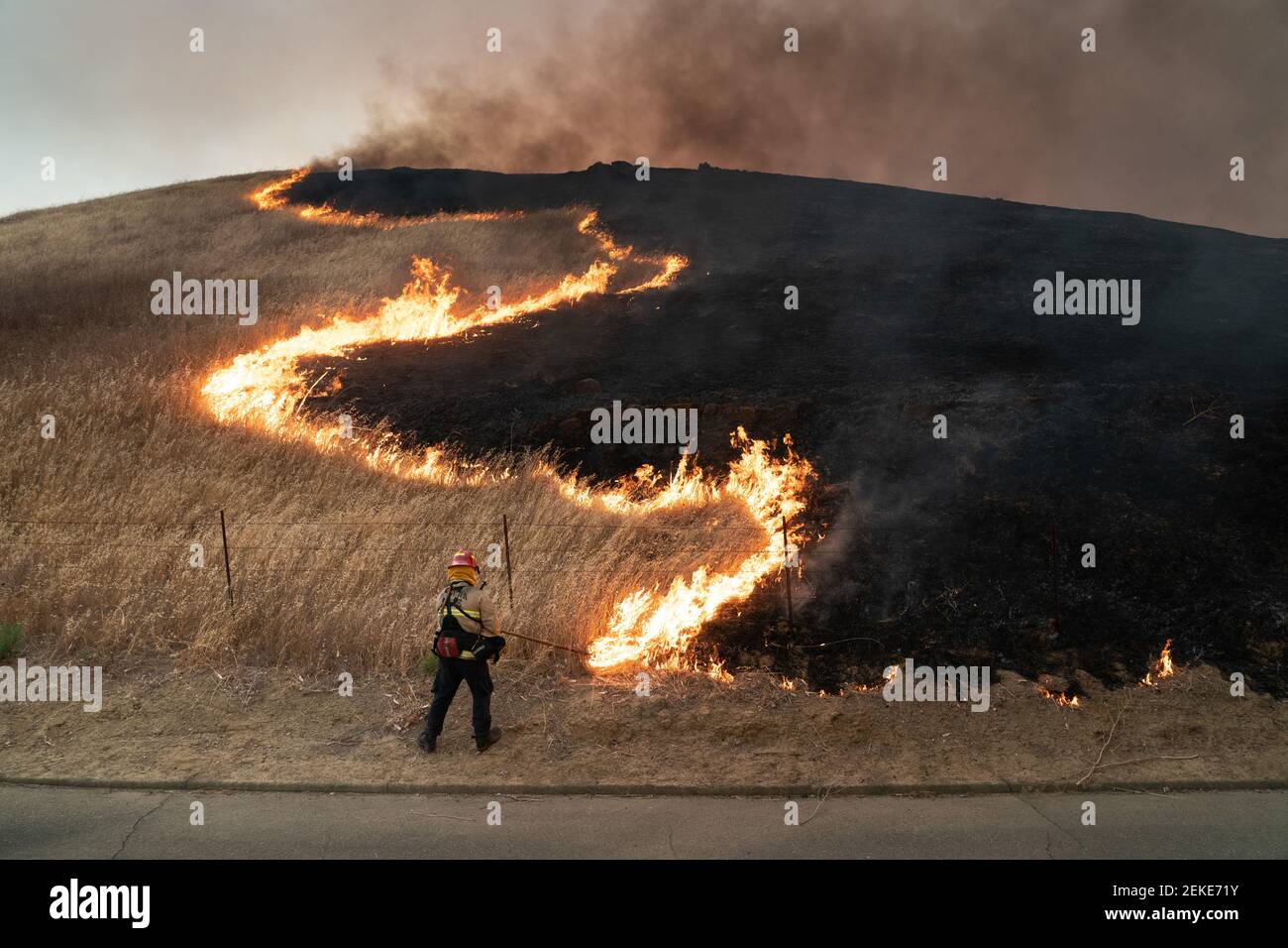 A firefighter rakes dry vegetation to the backfire during the Lightning ...