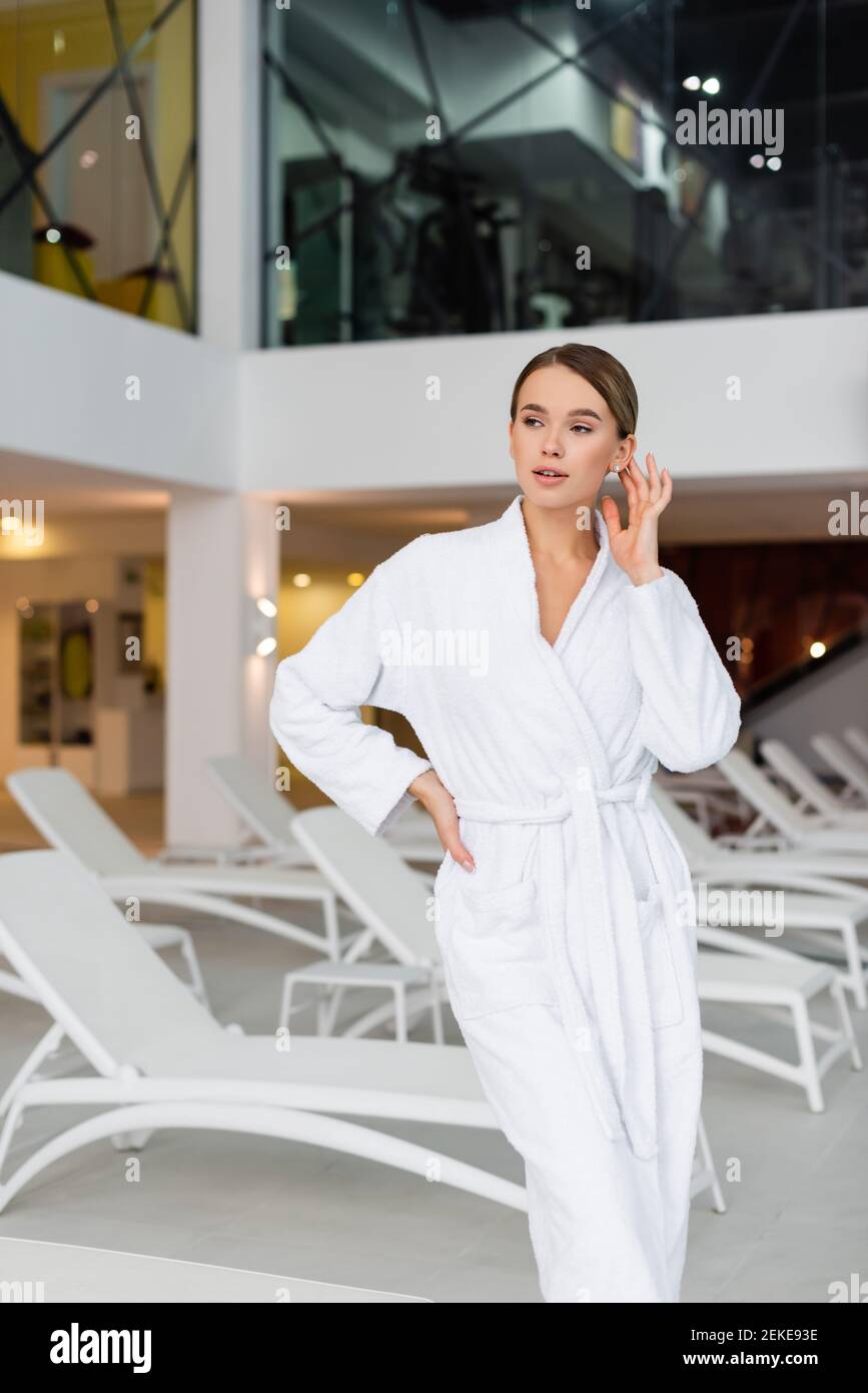young woman in white bathrobe standing with hand on hip near deck ...
