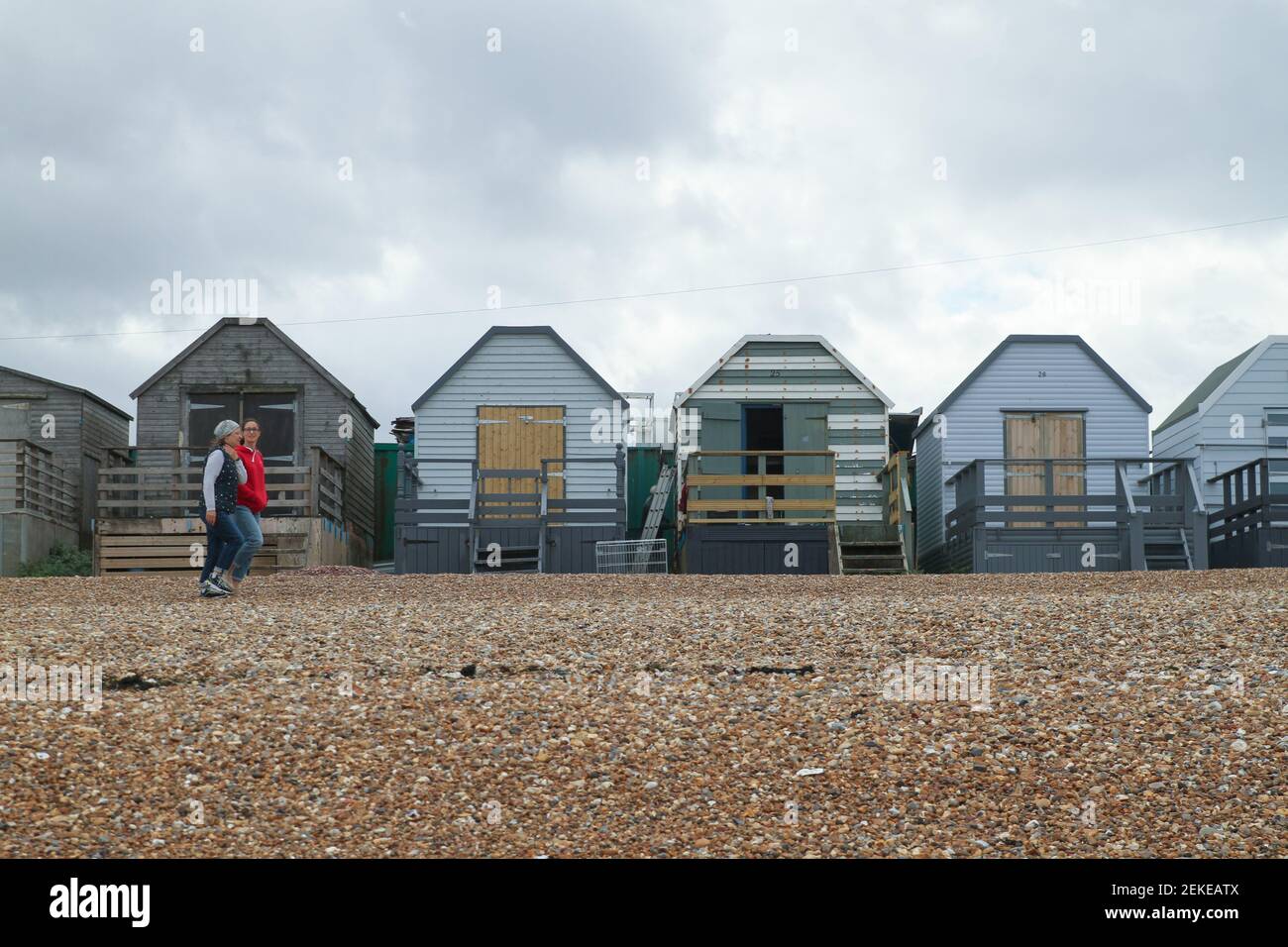 Two women walk by beach huts at the pebble beach in Whitstable on a ...
