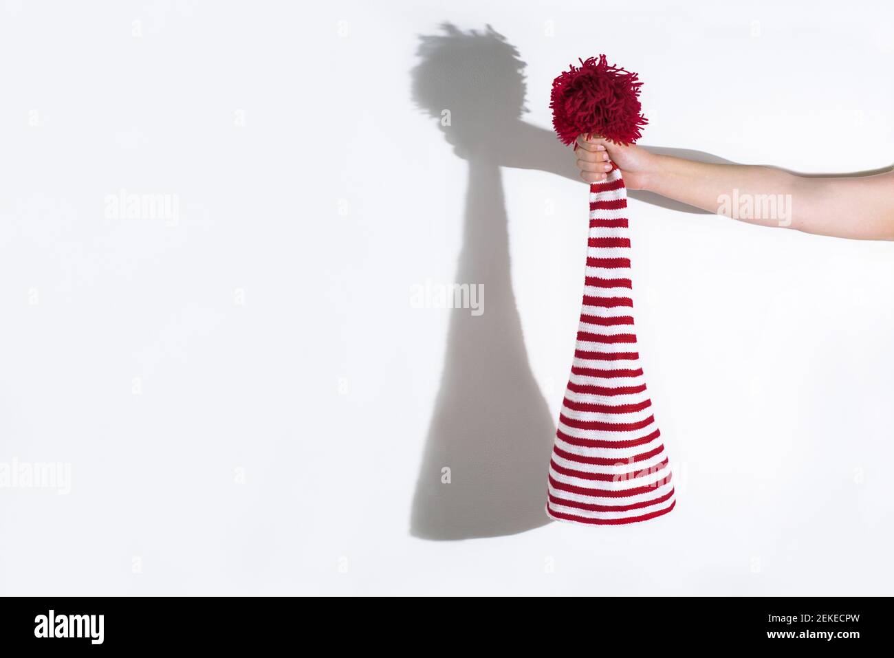One female hand holds a red striped cap with a large red pompom in hard ...