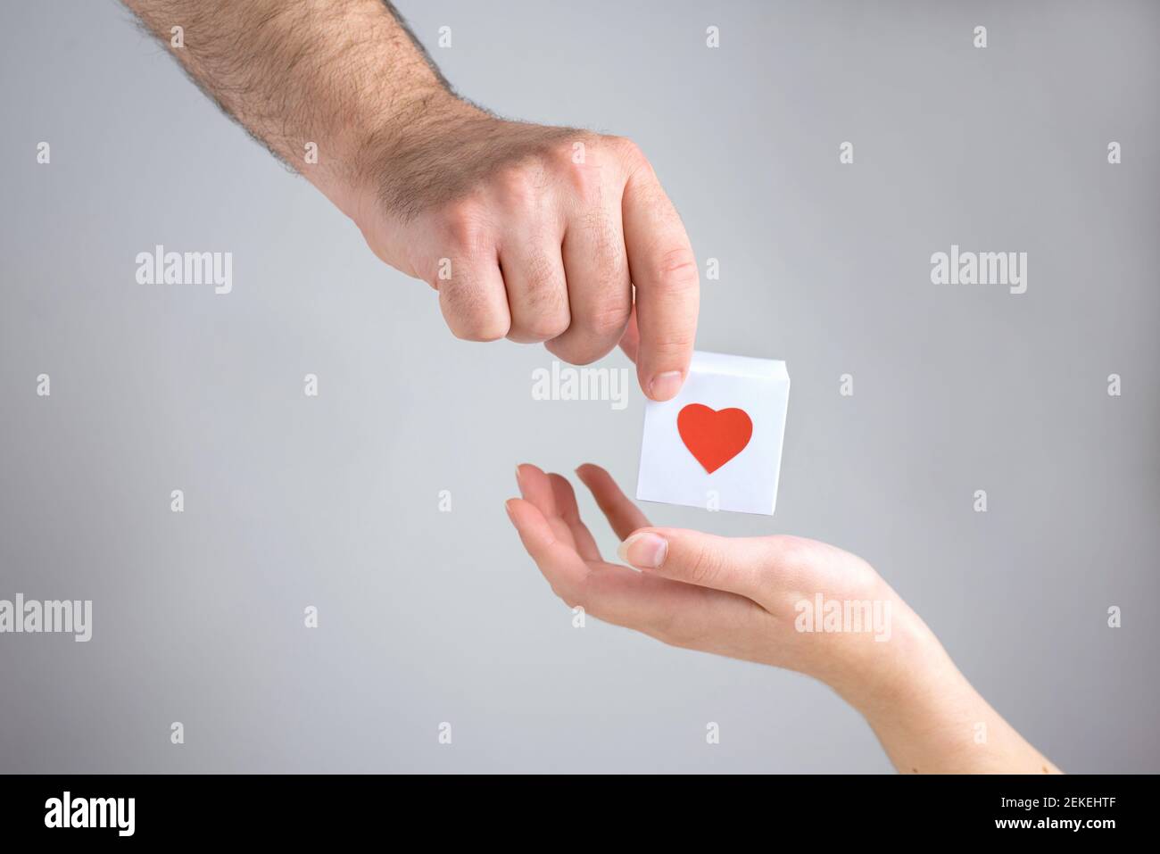One male hand gives to one female hand a white box with a heart, simbol ...