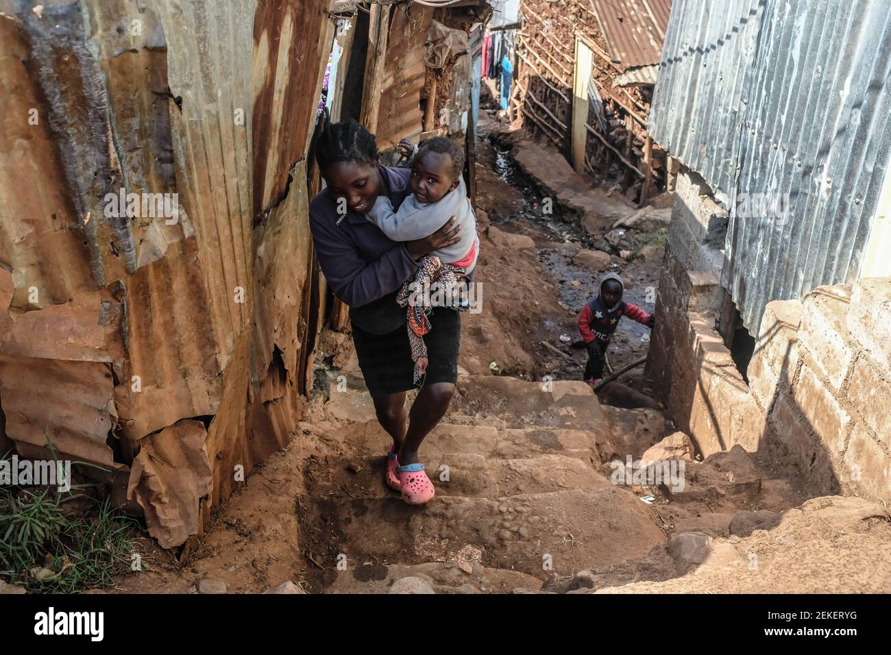 A woman and her little child walk past their home in Kibera Slums ...