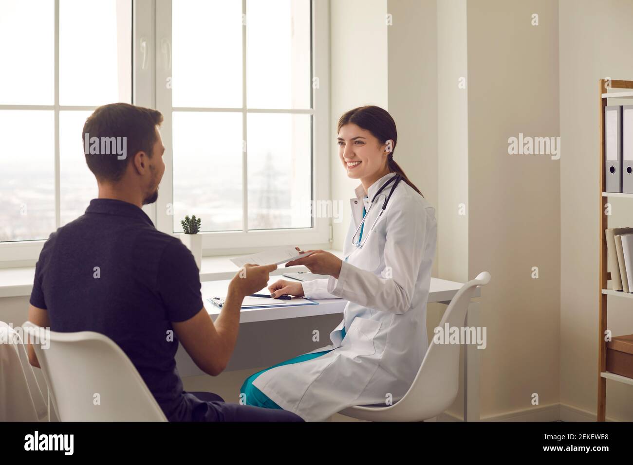 Positive woman medical worker sitting and giving paper prescriprion to ...