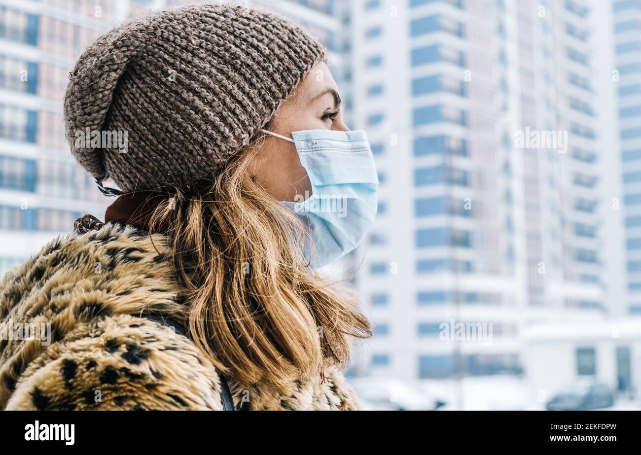 Young woman wearing protective mask, looking away at modern city street ...