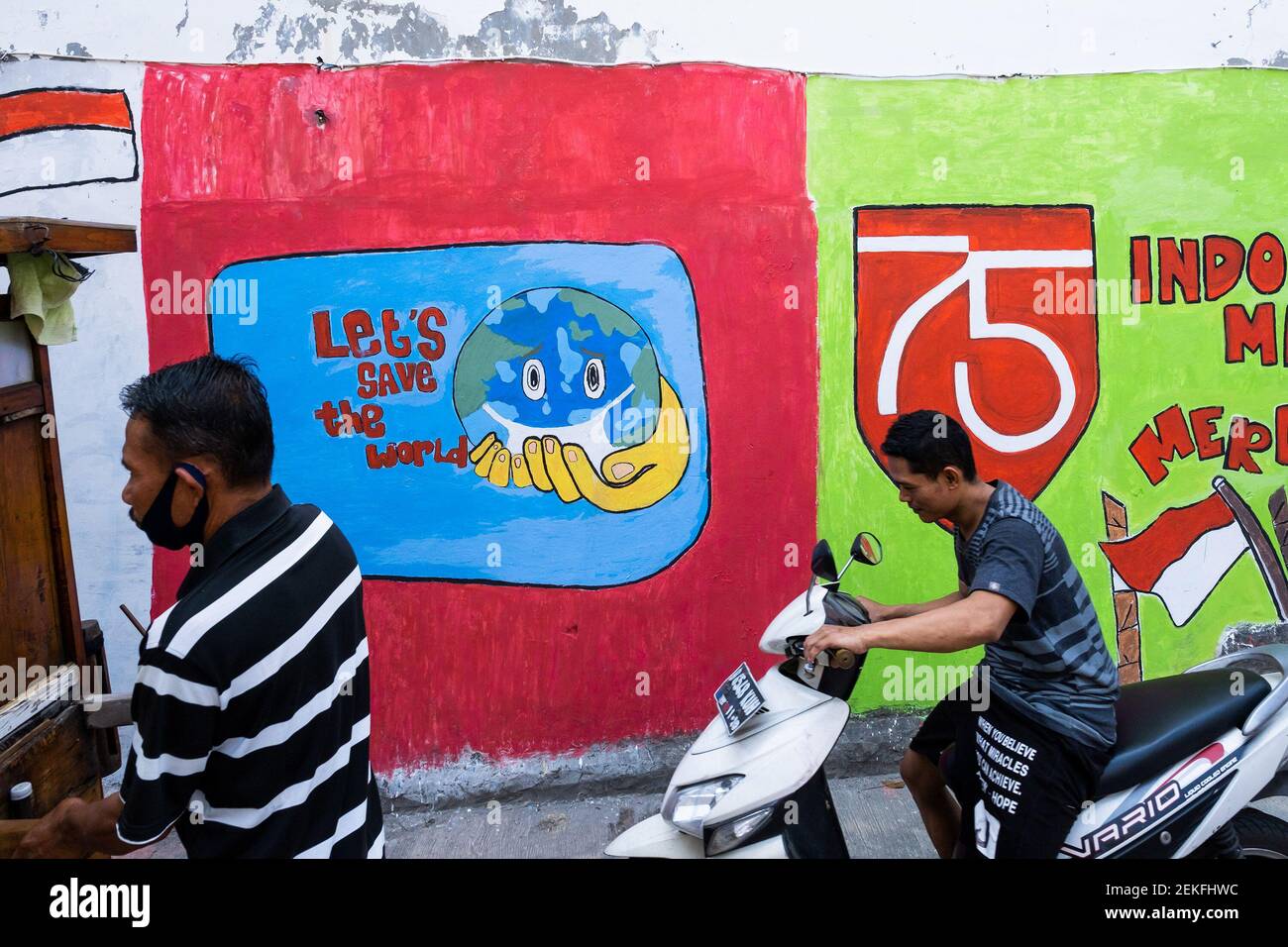 People passes a Covid-19 awareness mural on a wall, in Bekasi ...