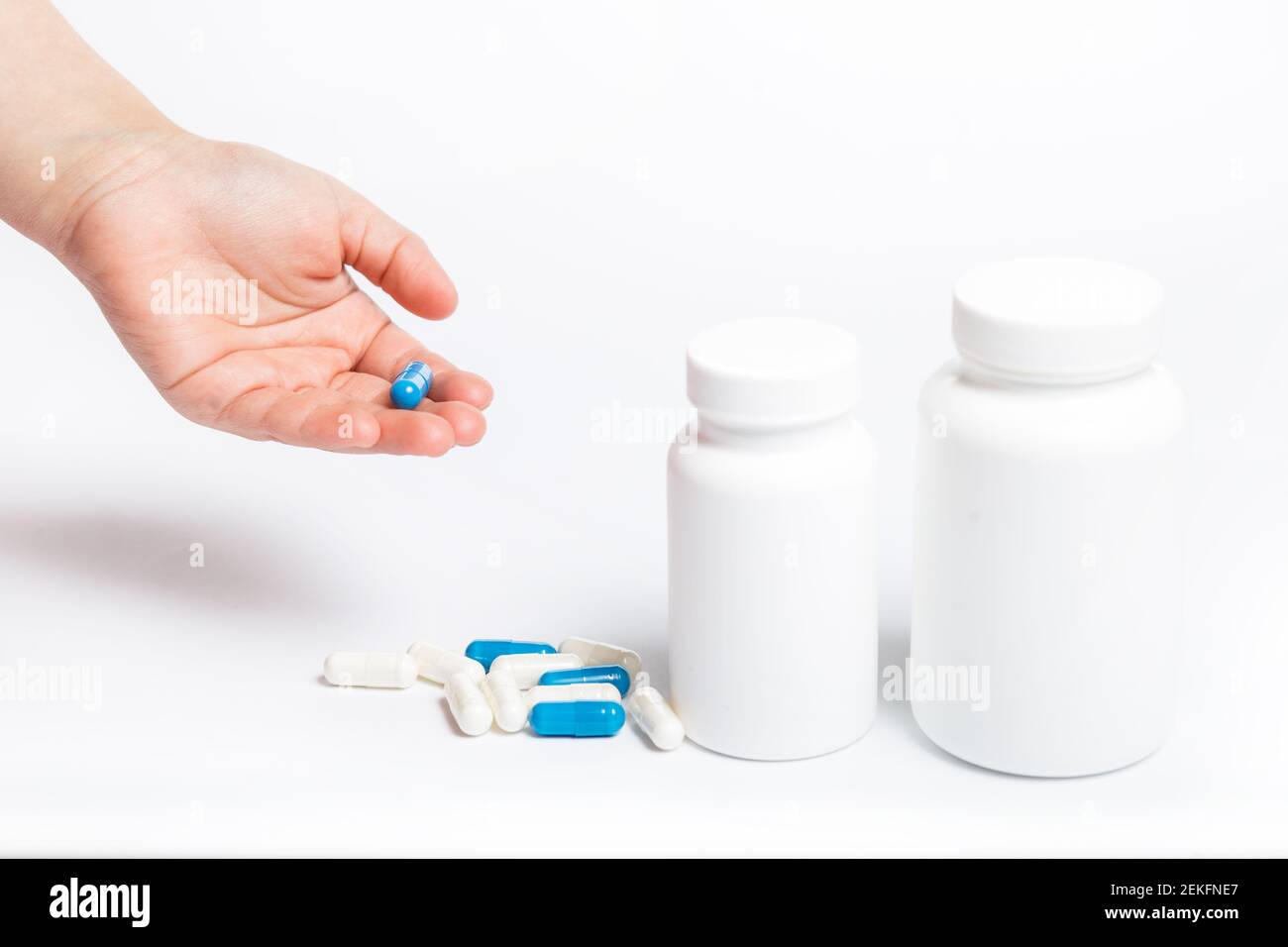 Child hand pick a blue pill from container on a white background with ...
