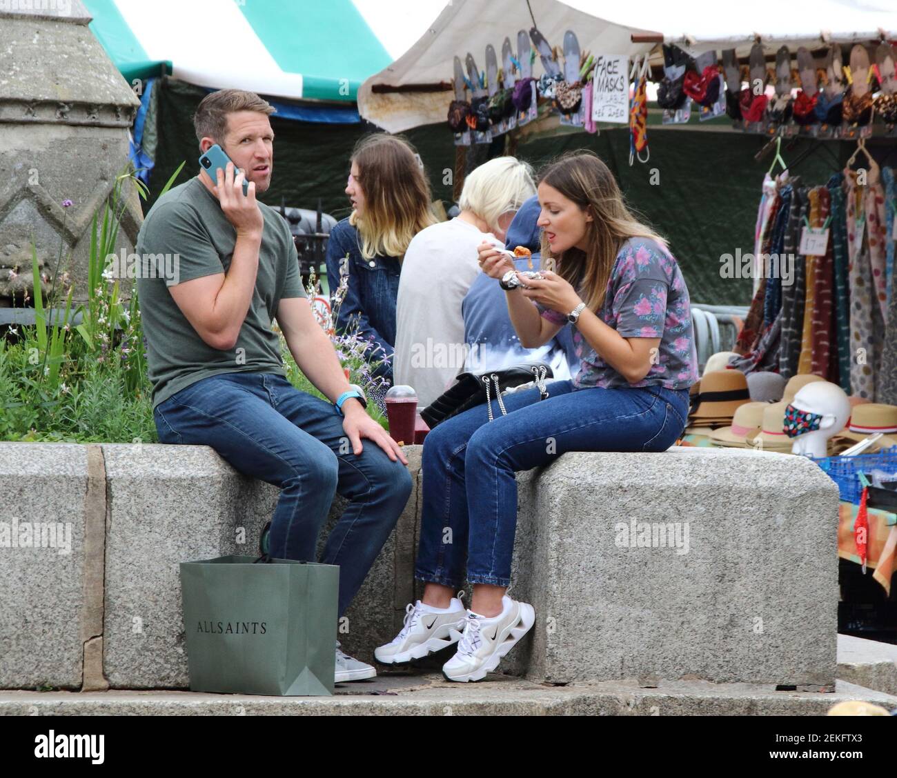 A man communicating on a mobile phone while a woman eats a takeaway in ...