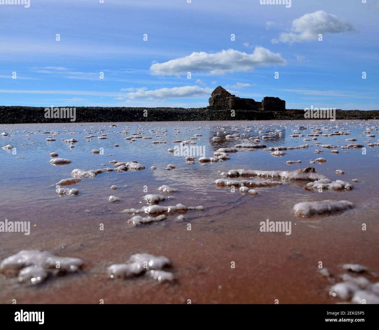 Salt lagoon in foreground, old construction and blue sky with clouds in ...