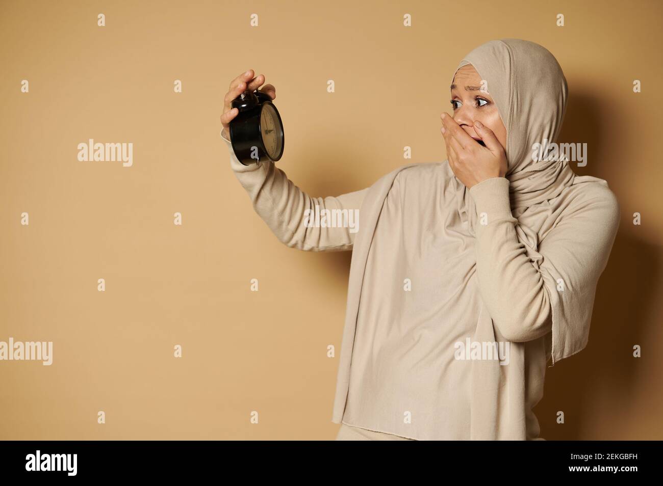 A stunned Arab woman with a covered head in a hijab holds an alarm ...