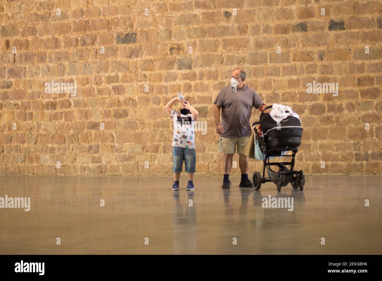 A man standing next to a baby stroller with his child drinking water in ...