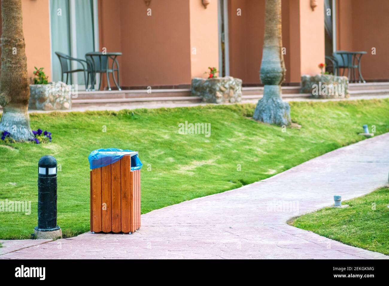 Yellow wooden trash can outdoors on the side of sidewalk in park ...