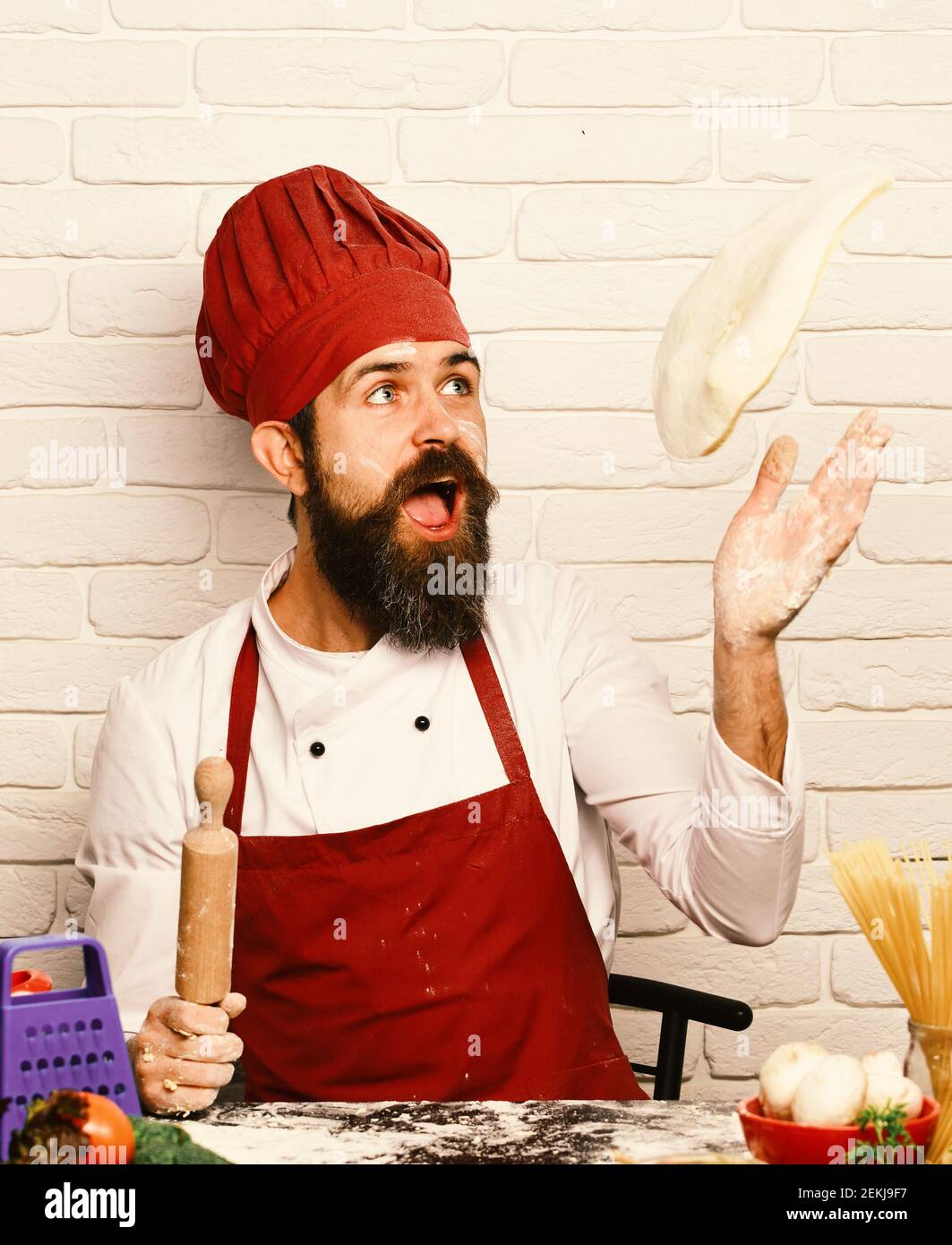 Man with beard throws pizza dough up on white brick wall background ...