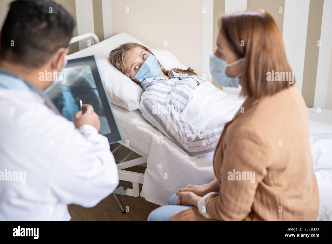Young blond sick woman in protective mask looking at her doctor and ...