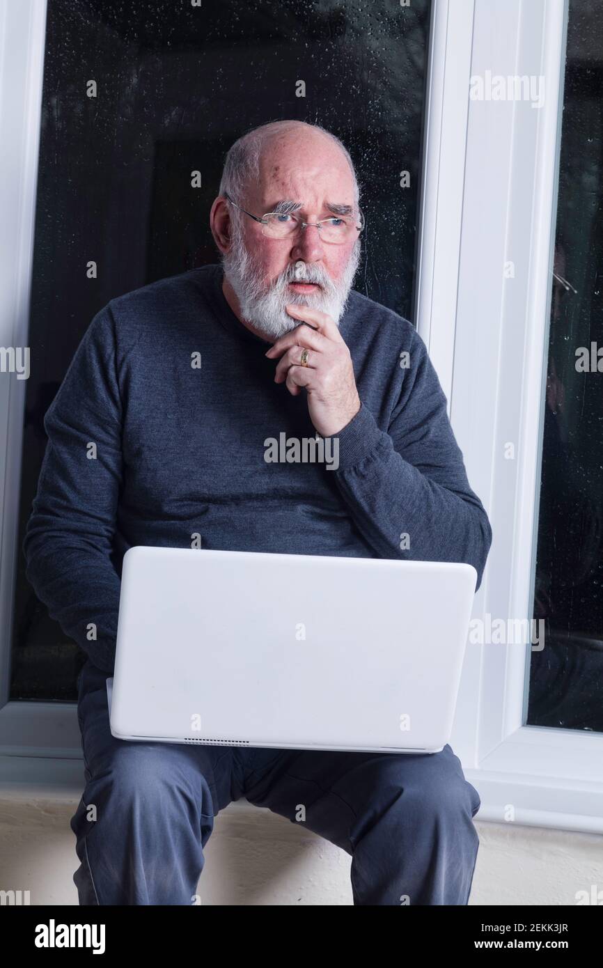 Elderly man sitting in his conservatory at night trying to use a laptop ...