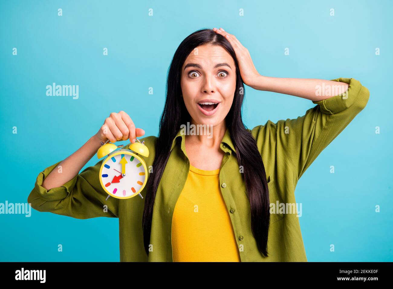 Photo of amazed girl hold alarm clock hand head excited wear green ...