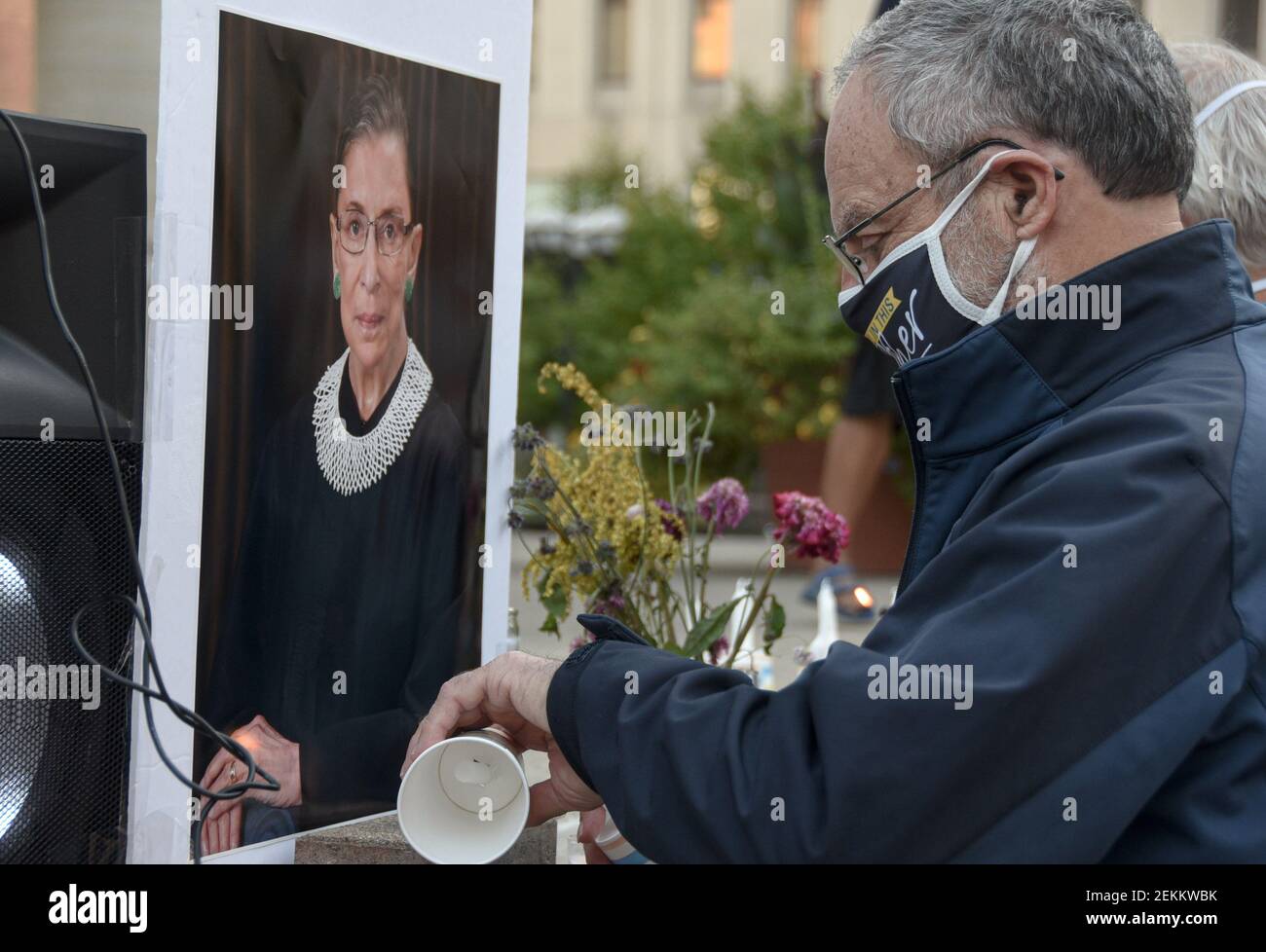 A mourner wearing a face mask lights a candle during a vigil honoring ...