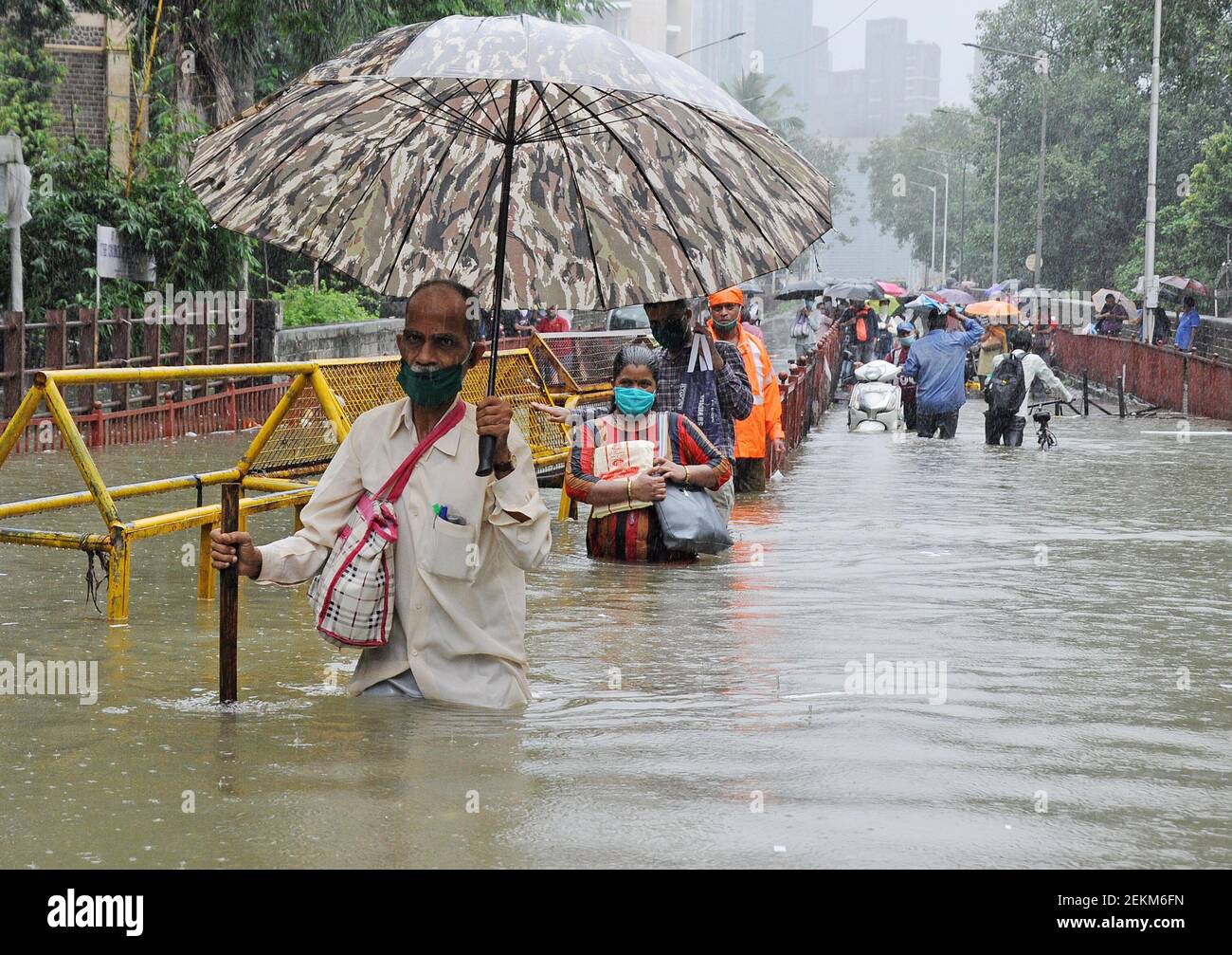 A man holding an umbrella and a walking stick wade through waist deep ...