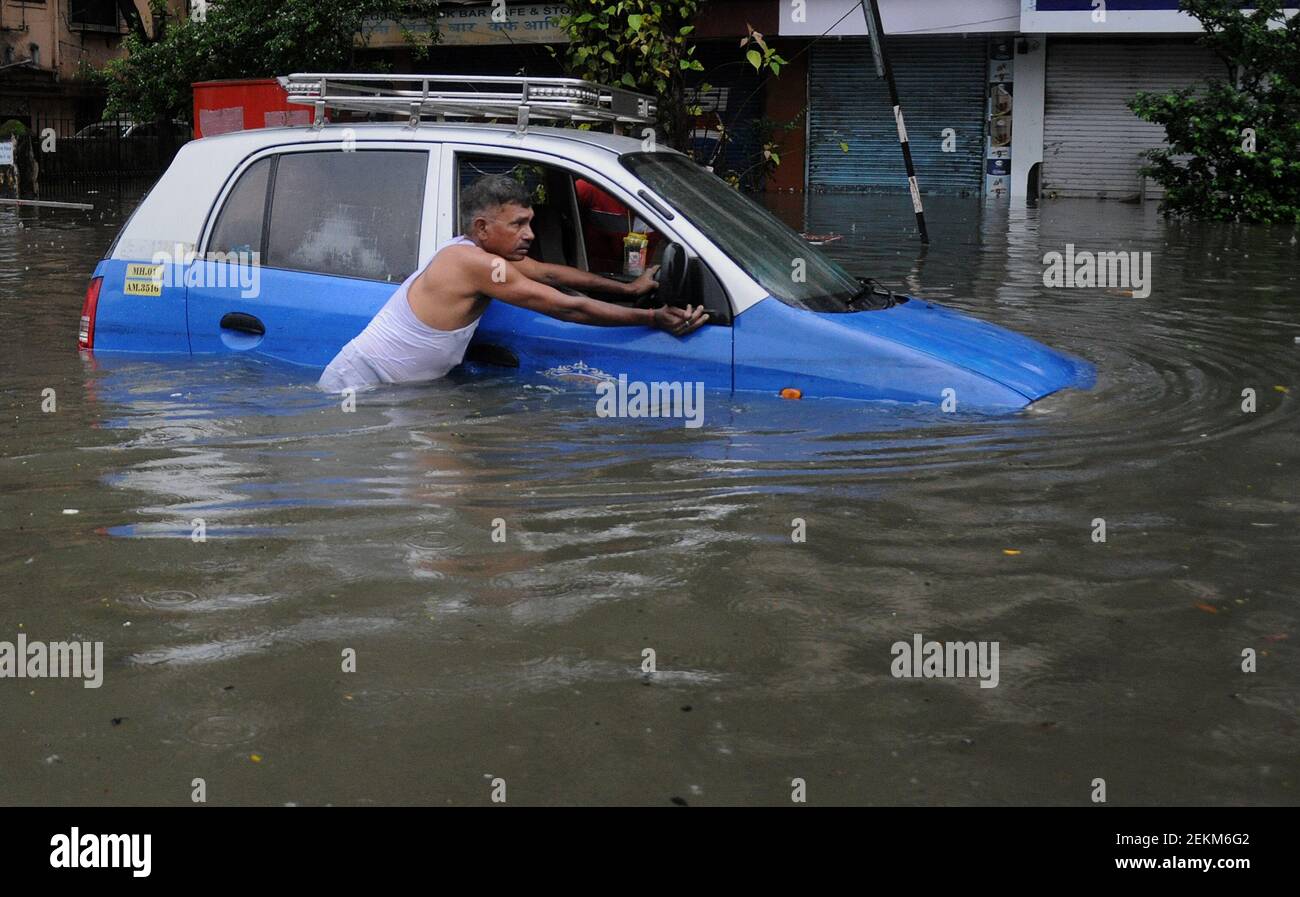 A man pushes tries to push his car on a waterlogged road. Heavy rains ...
