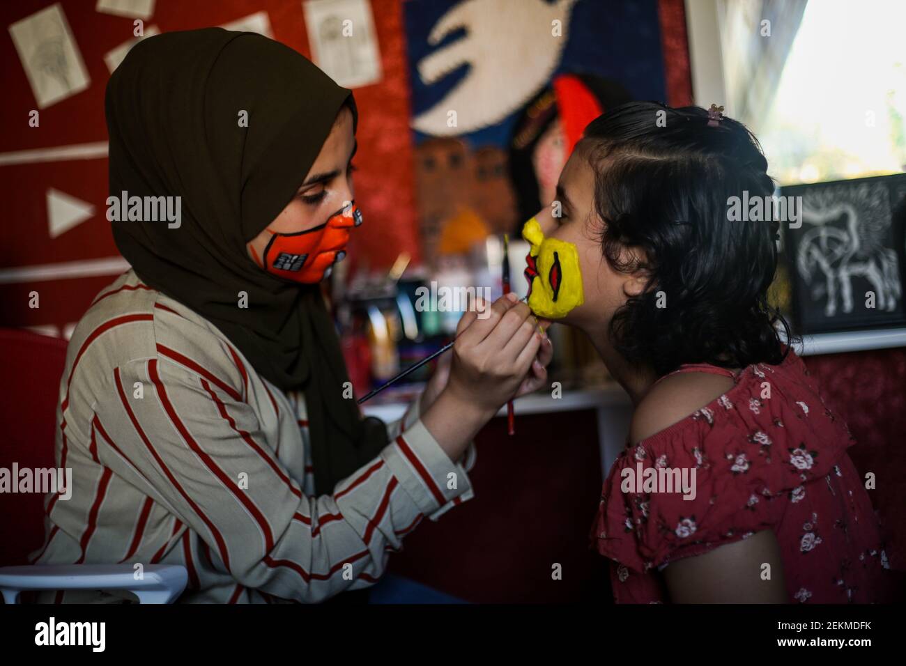 Palestinian girl uses water paint as paints a mask a young girl's face ...