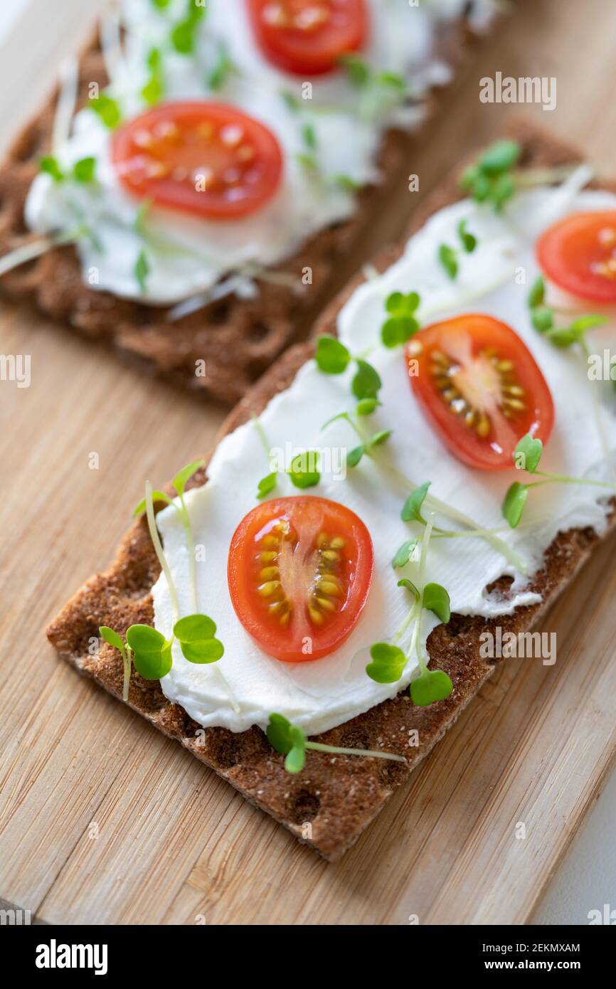 Rye crisp bread with creamy vegetarian cheese, cherry tomato and rucola ...