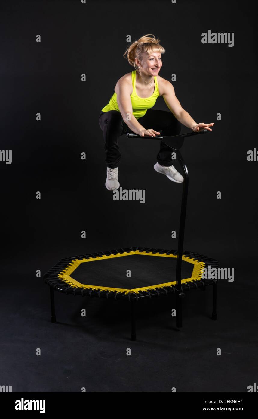 Girl on a fitness trampoline on a black background in a yellow t-shirt ...