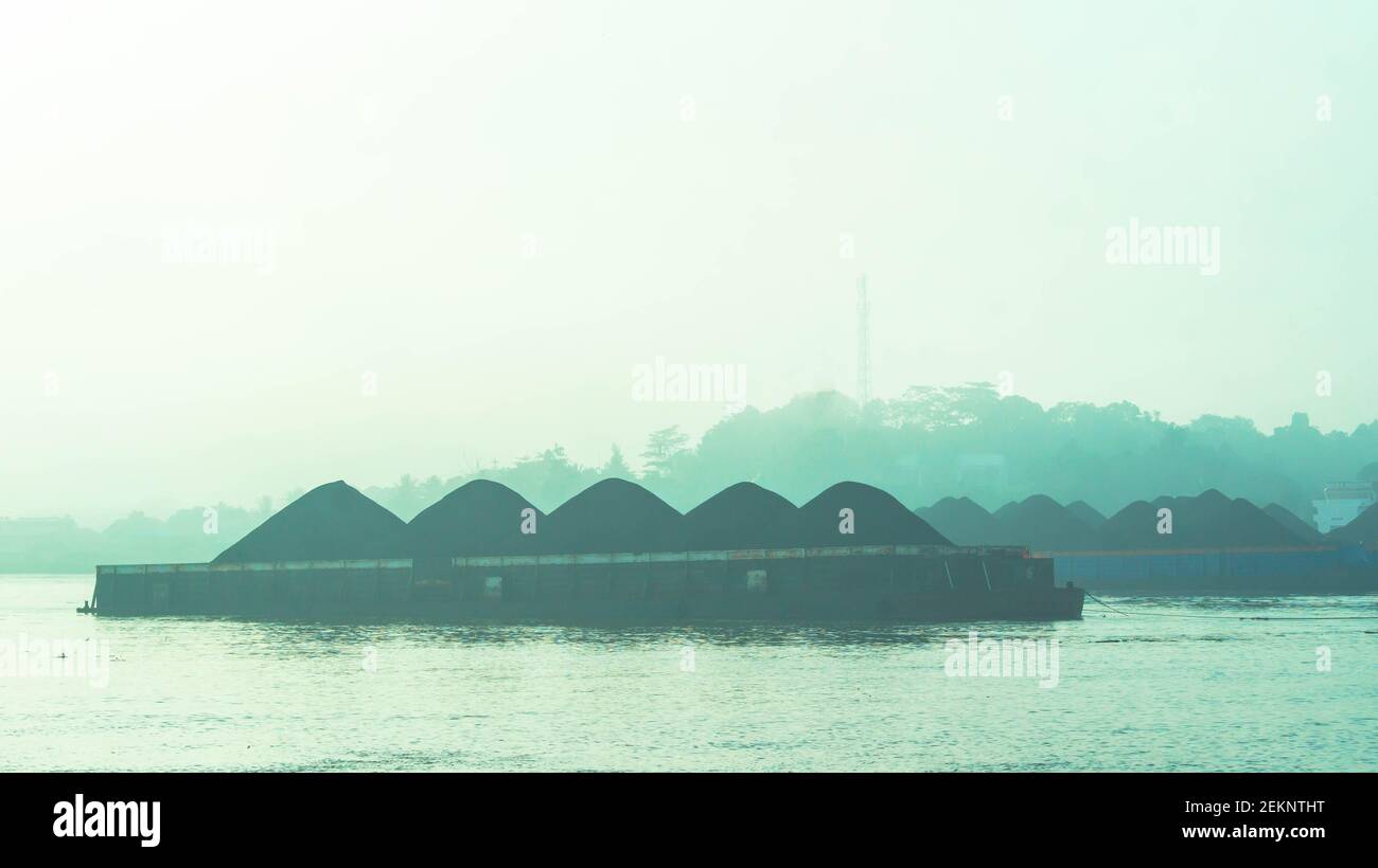 Misty morning in Mahakam river, tugboat dragging barge full of coal ...